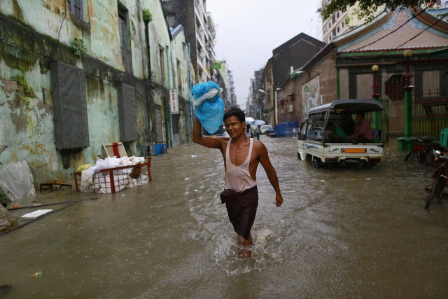 A man carries a bag as he walks along a flooded street during heavy ...